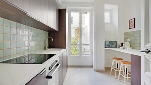 Uma cozinha moderna com fogão espaçoso, armários brancos e janela com vista para uma varanda.