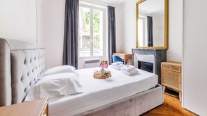 Quarto de hotel com uma cama, um espelho grande, lareira e janela com cortinas.