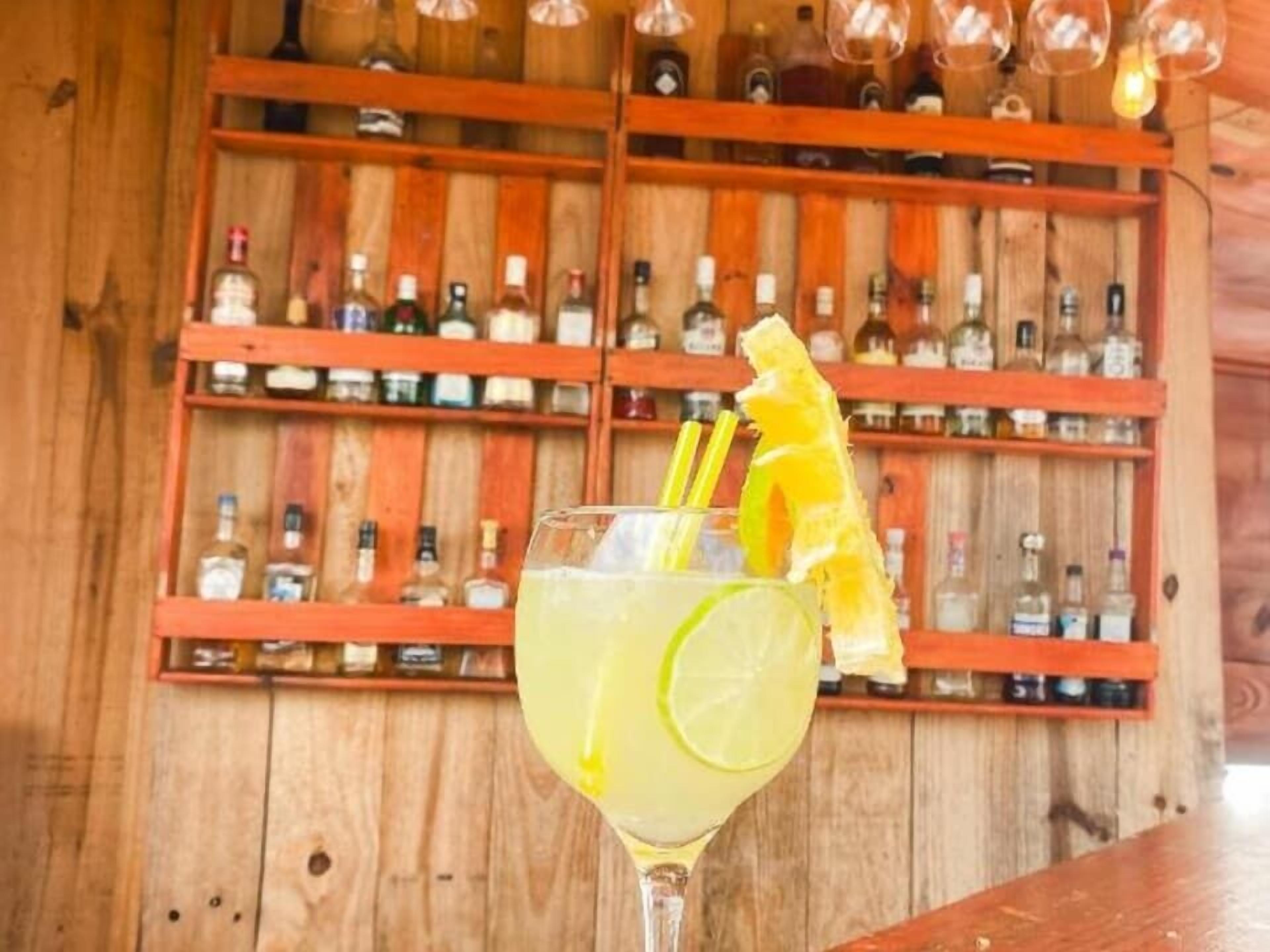 Uma área de bar com prateleiras de garrafas de bebidas e um copo de coquetel com uma fatia de limão e canudo.