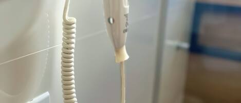 Um secador de cabelo branco fixado na parede, com o fio enrolado.