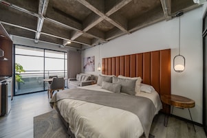 Quarto de hotel moderno com uma cama grande, um sofá, uma mesa de jantar e vista para o exterior.