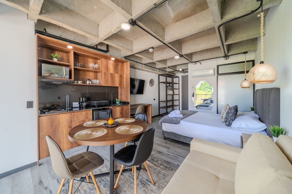 Uma cozinha moderna com armários de madeira, uma mesa de jantar com cadeiras, uma cama com vista e um lustre.