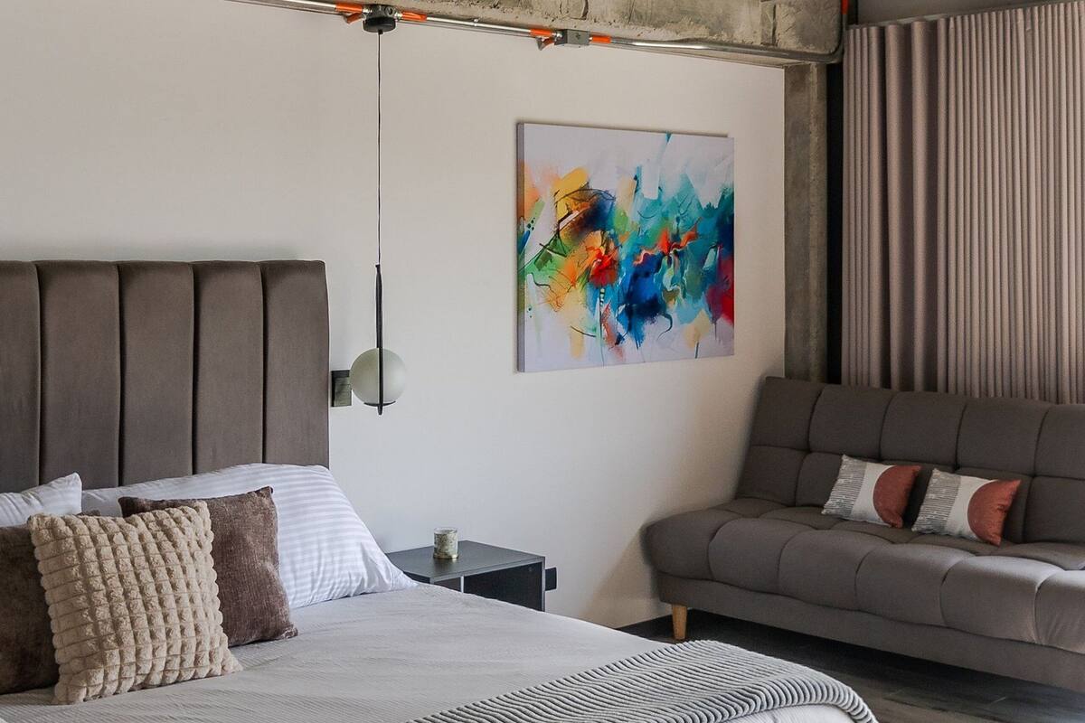 Um quarto moderno com uma cama grande, um sofá e uma pintura abstrata colorida.