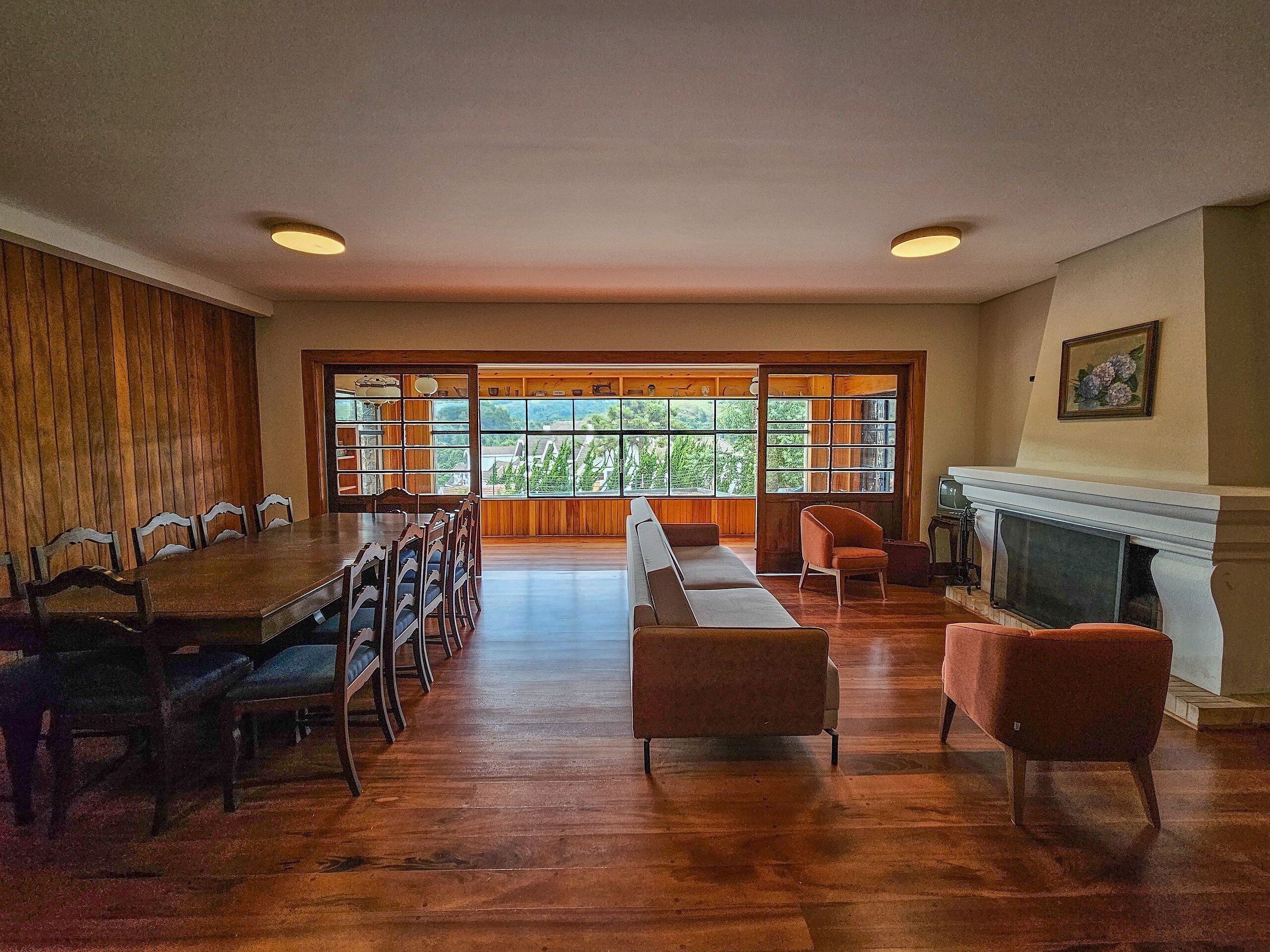 Uma sala de estar ampla com uma mesa de jantar de madeira, várias cadeiras, um sofá e uma lareira.