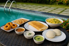 Uma mesa com uma variedade de pratos indianos, incluindo um crepe enrolado, dois tipos de pão, uma tigela de arroz e várias pequenas tigelas de sopa e chutney.