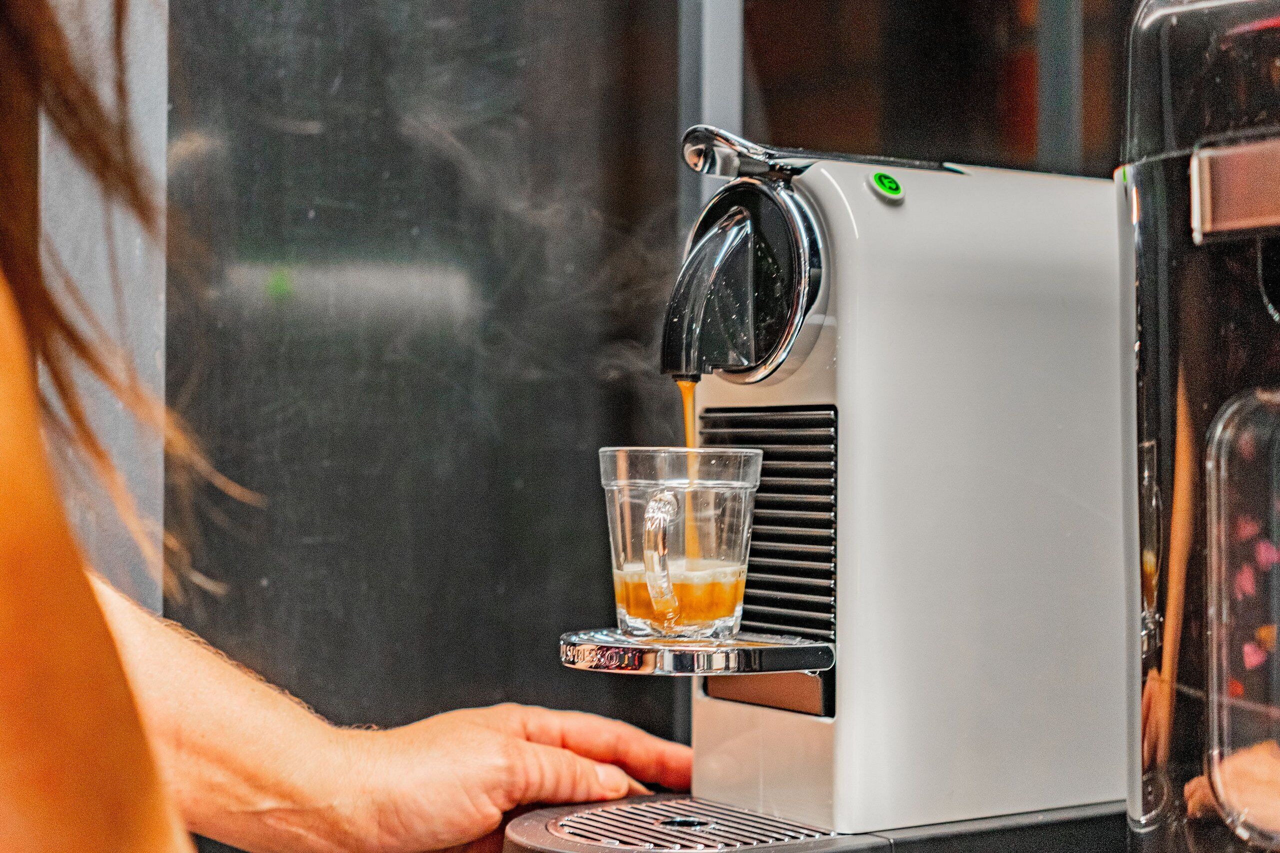 Alguém opera uma máquina de café, servindo café em um copo.