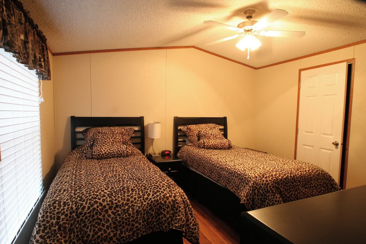 Quarto com duas camas, um ventilador de teto e uma porta.