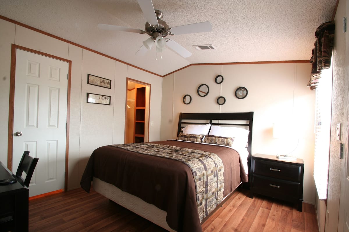 Quarto com cama, mesa de cabeceira, ventilador de teto, porta e parede com detalhes circulares.