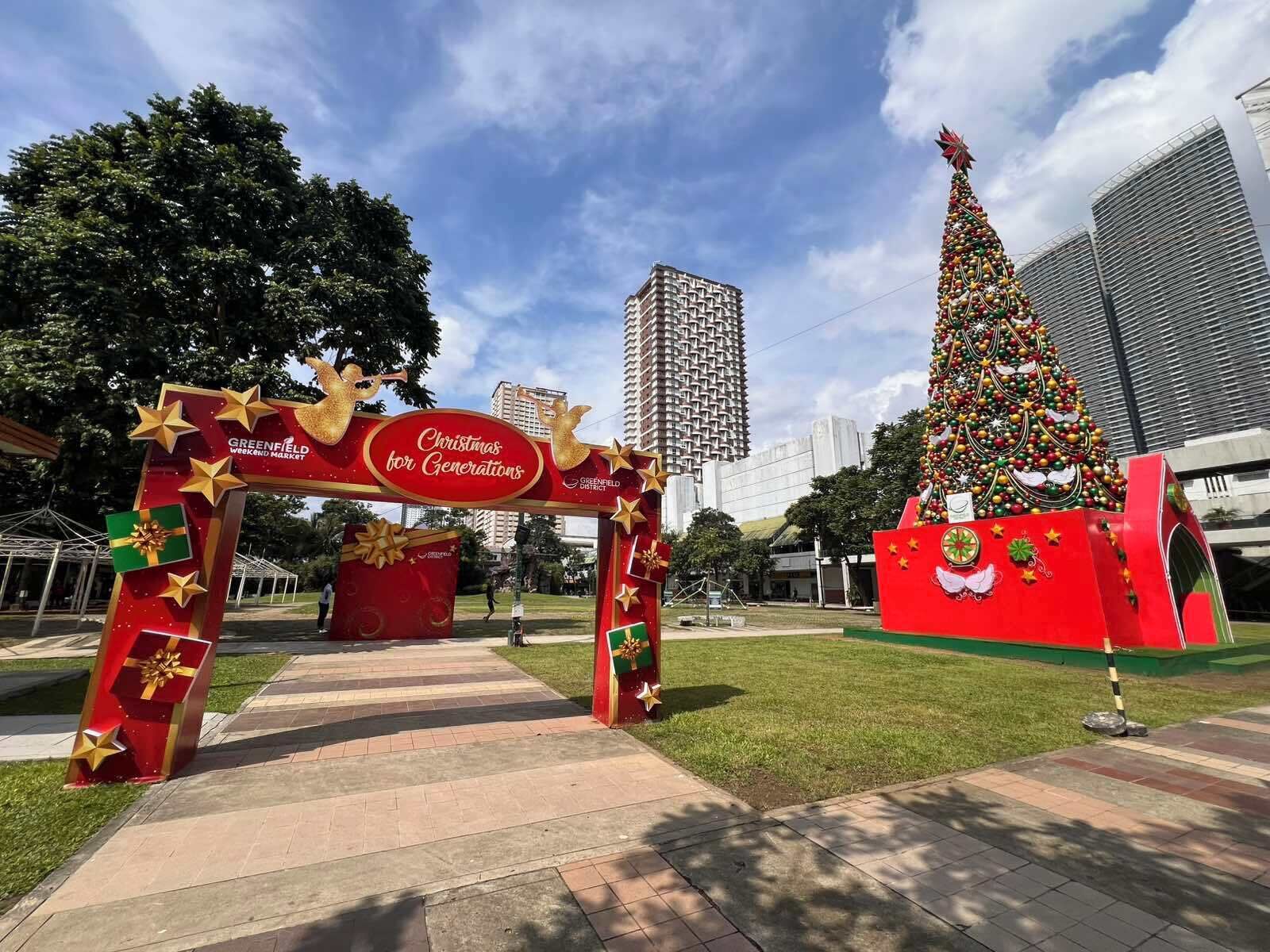 Entrada de um mercado de Natal, com um arco decorado e uma grande árvore de Natal.