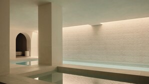 Uma área de piscina interior moderna, com parede texturizada e piscina transparente.