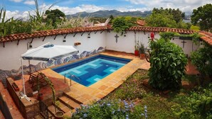 Piscina com deck ladrilhado, cercada por um muro branco com azulejos decorativos e plantas.