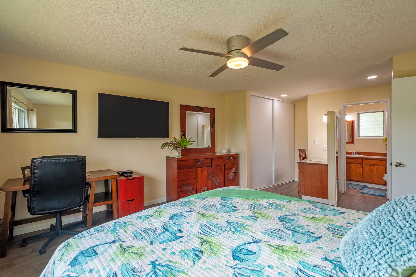 Quarto com cama, escrivaninha, cadeira, cômoda, espelho e ventilador de teto.