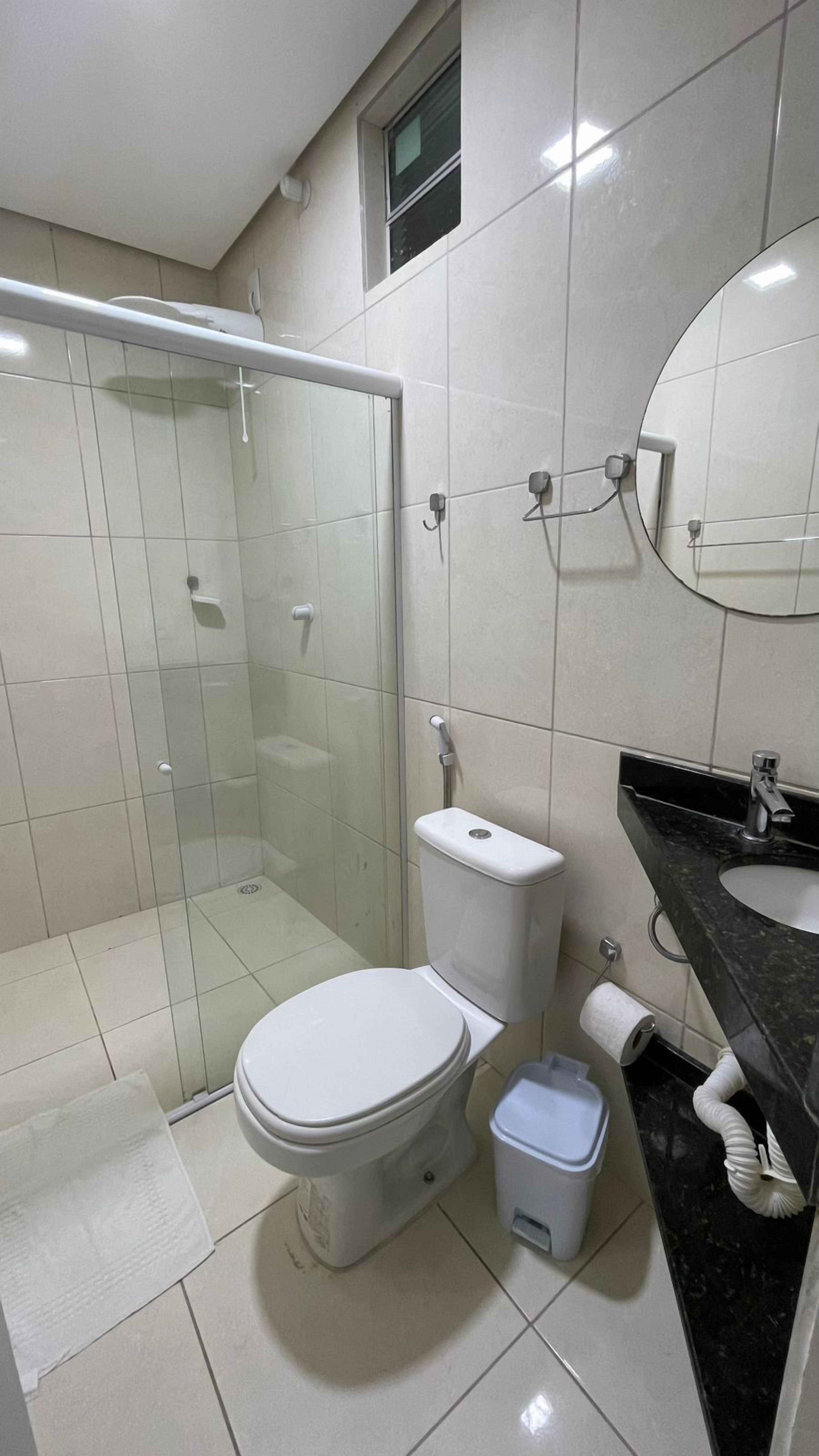 Uma casa de banho moderna com cabine de duche em vidro, sanita, lavatório e espelho.