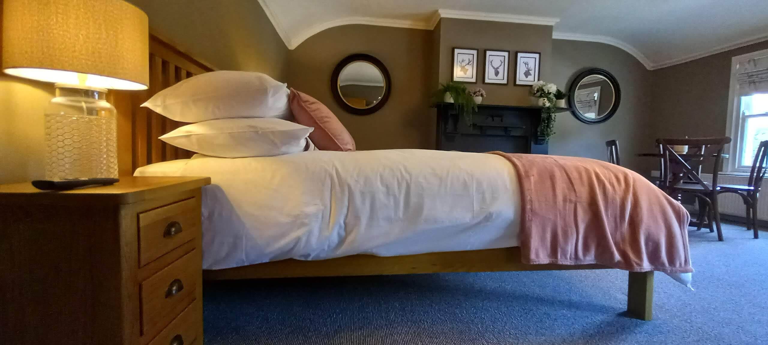 Quarto com cama, mesa de cabeceira, luminária, cômoda e lareira.