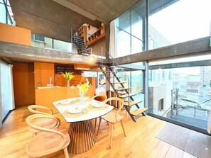 Uma sala de jantar moderna com uma mesa de madeira, cadeiras e vista da cidade através de grandes janelas.