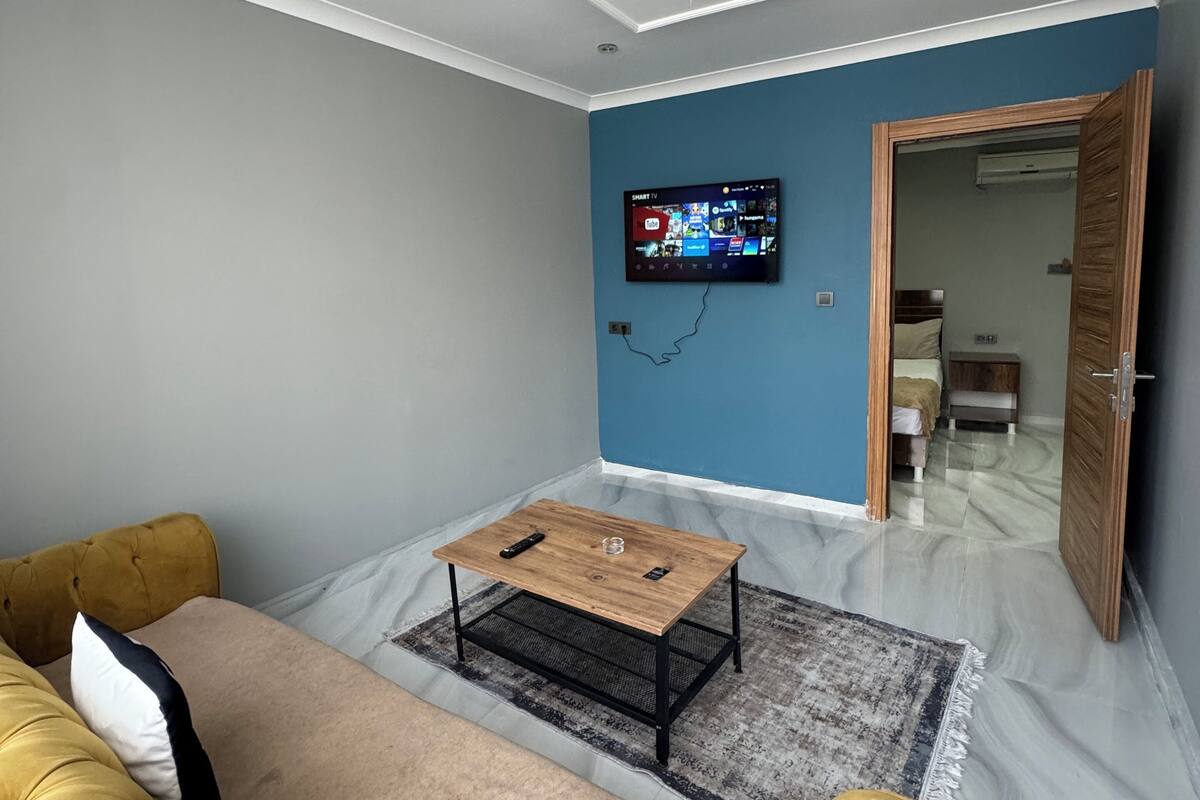 Uma sala de estar moderna com um sofá, uma mesa de centro e uma TV fixada na parede.