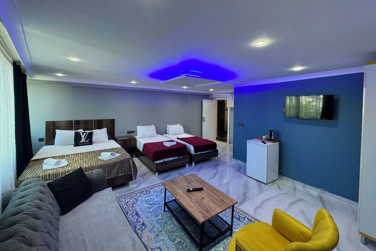 Quarto de hotel moderno com duas camas, um sofá, uma mesinha, uma TV e um minibar.
