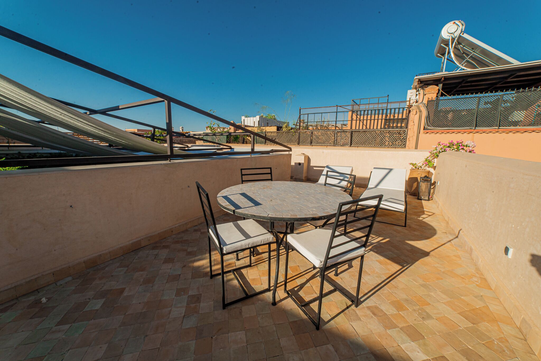 Um terraço no telhado com uma mesa redonda e cadeiras, uma antena parabólica e vista para a paisagem urbana.