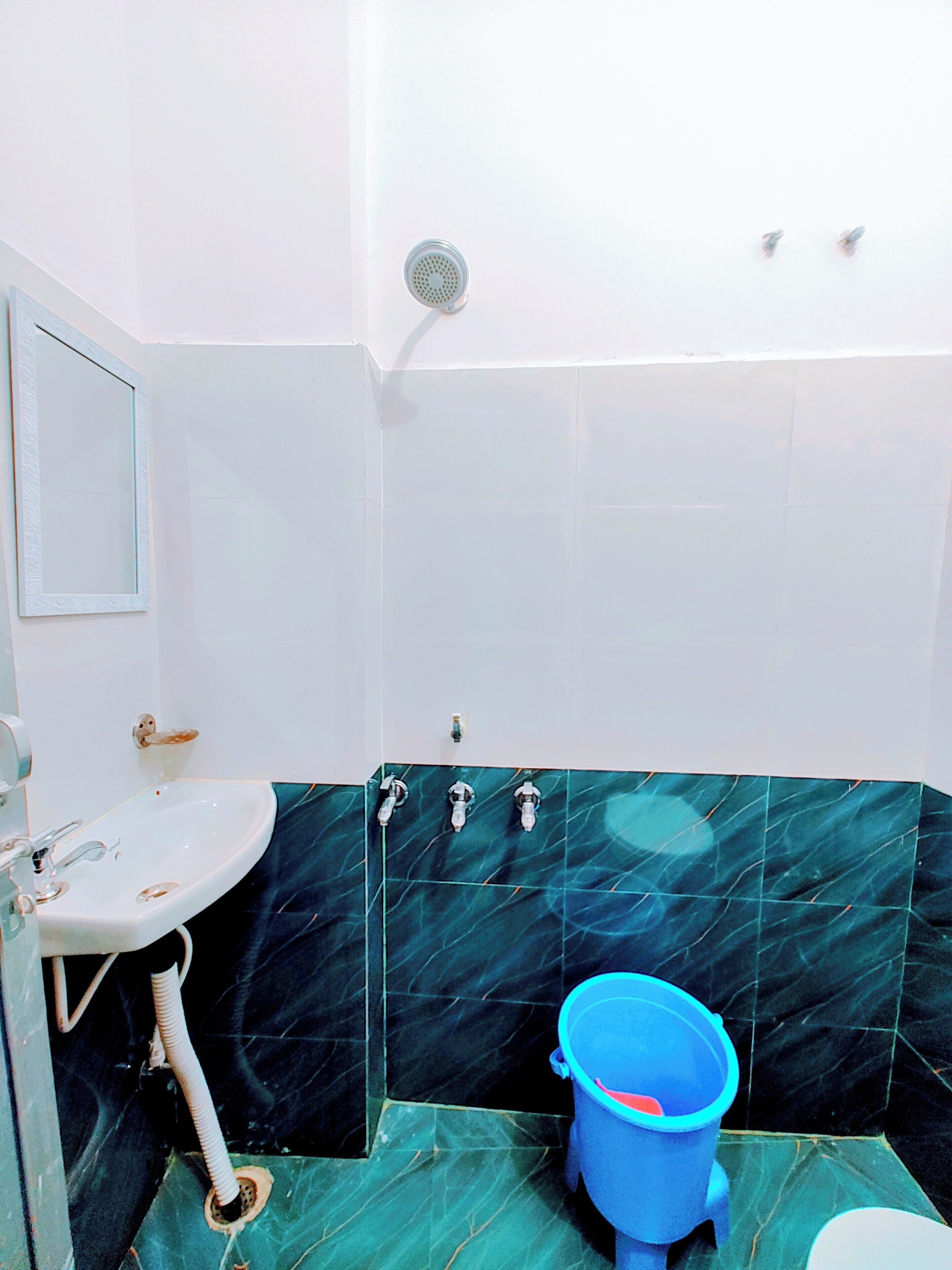 Casa de banho com lavatório, três torneiras, um balde azul e azulejos de mármore verde escuro.