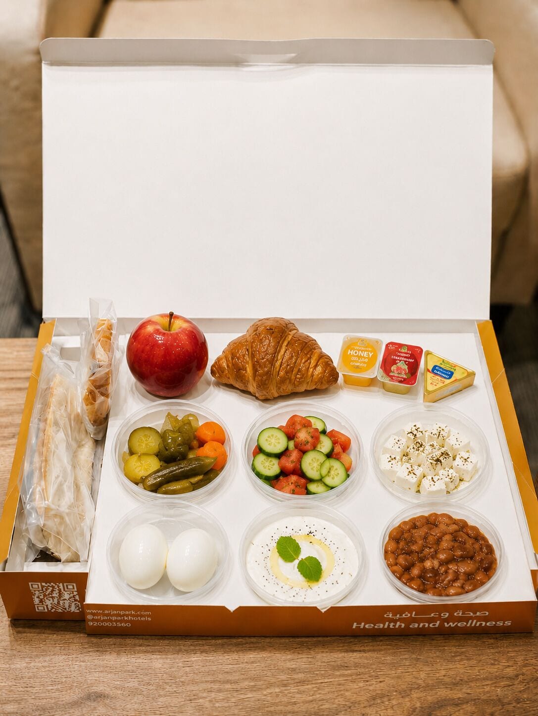 Caixa de refeição com croissant, maçã, queijo, iogurte e diversas saladas.