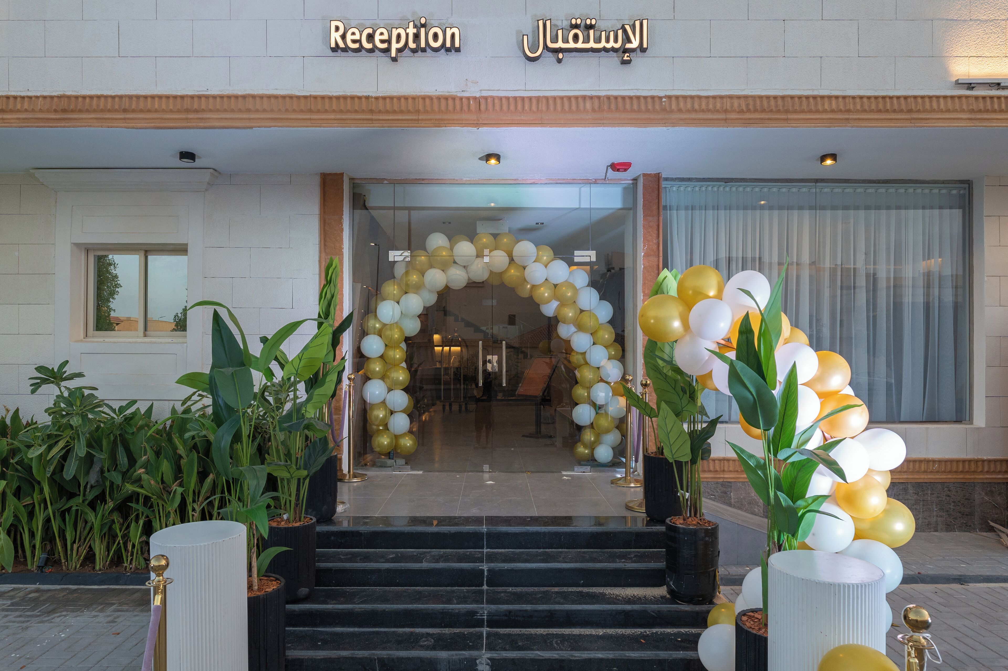 Entrada de hotel com balcão de recepção, escada que sobe e um arco decorativo de balões.