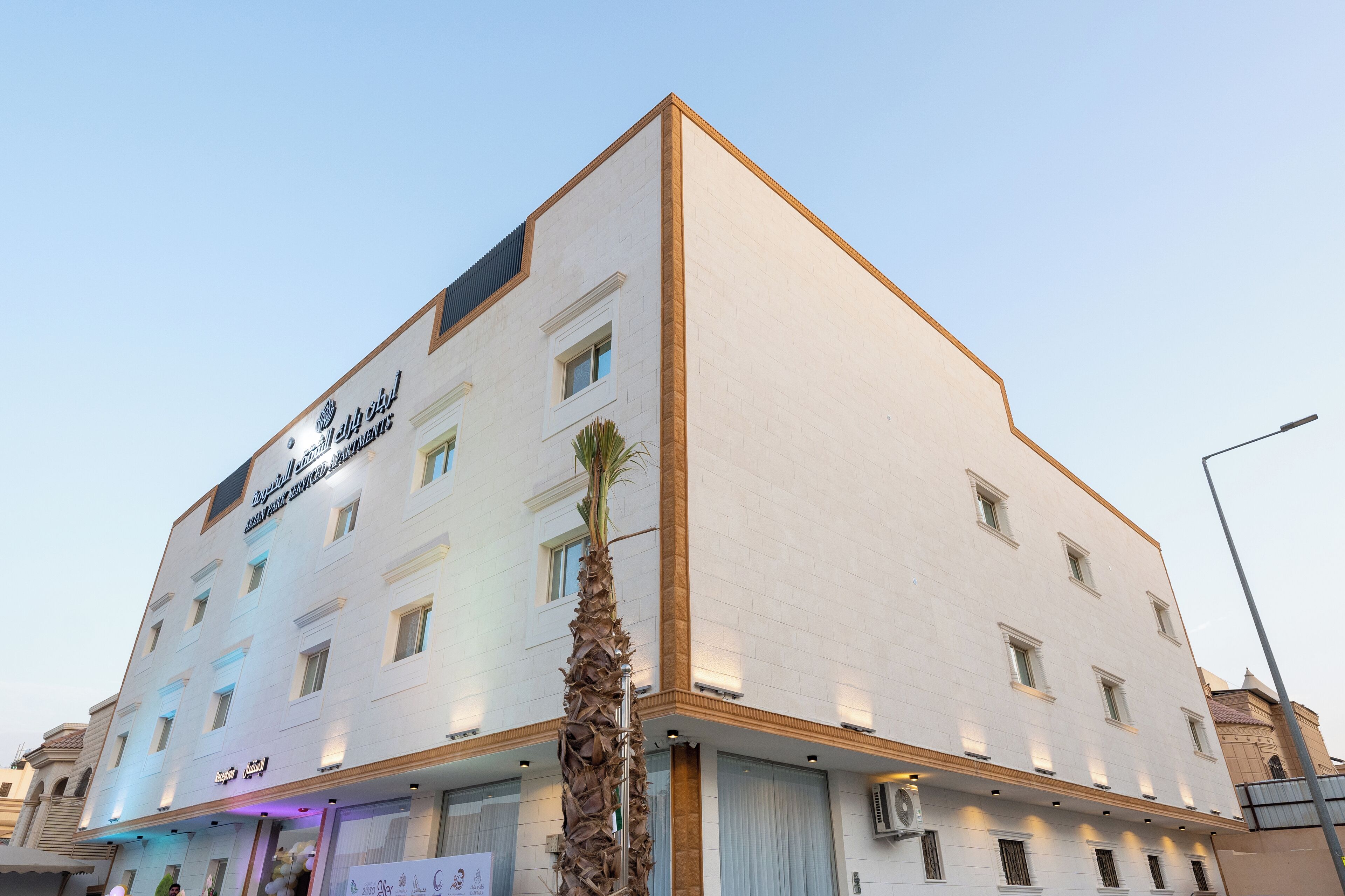 Um hotel com fachada branca, várias janelas e uma palmeira na frente.
