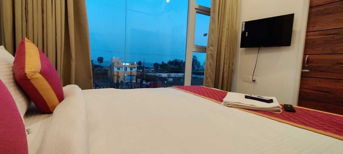 Quarto de hotel com cama, televisão fixada na parede e janela com vista para edifícios.