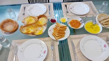 Mesa de café da manhã com pratos, talheres e diversos alimentos.