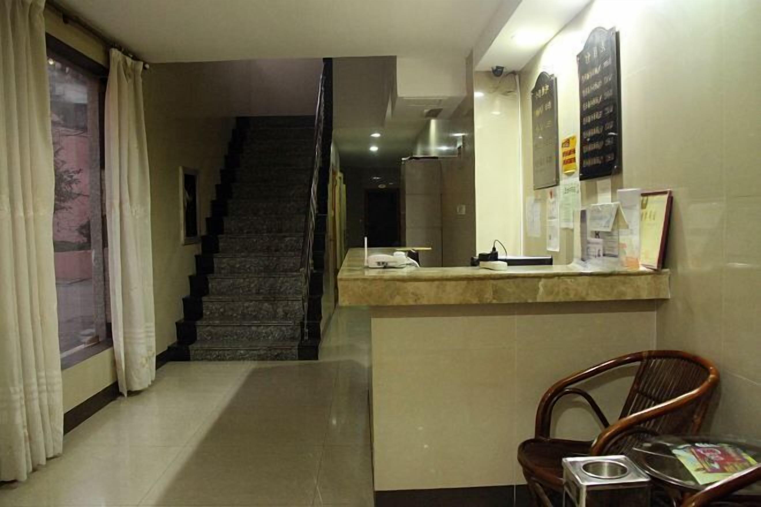 Uma área de recepção de hotel com balcão de mármore, uma escadaria e um espaço de refeições com cadeiras.