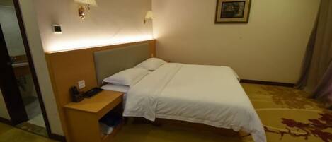 Quarto de hotel com cama, mesa de cabeceira, abajur e um quadro na parede.