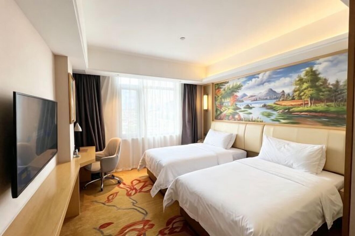 Quarto de hotel com duas camas, uma mesa, uma televisão e um quadro na parede.