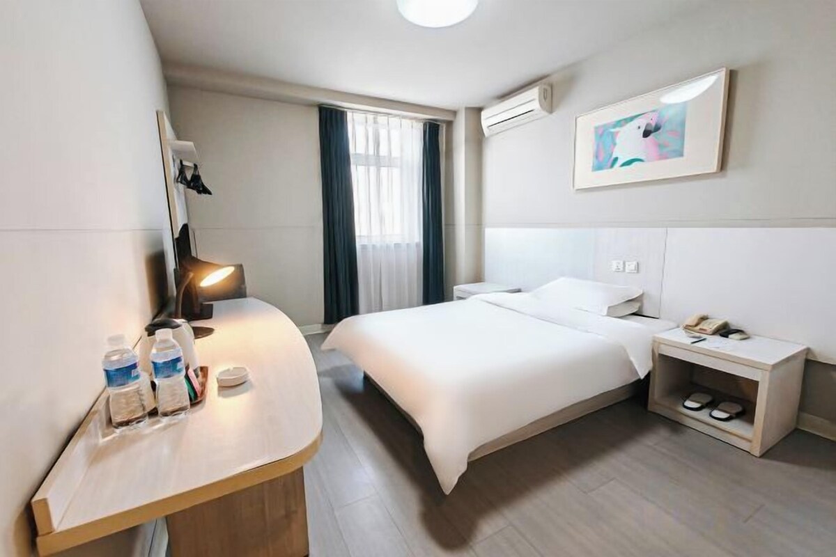 Quarto de hotel com cama, mesa de cabeceira e escrivaninha com cadeira.