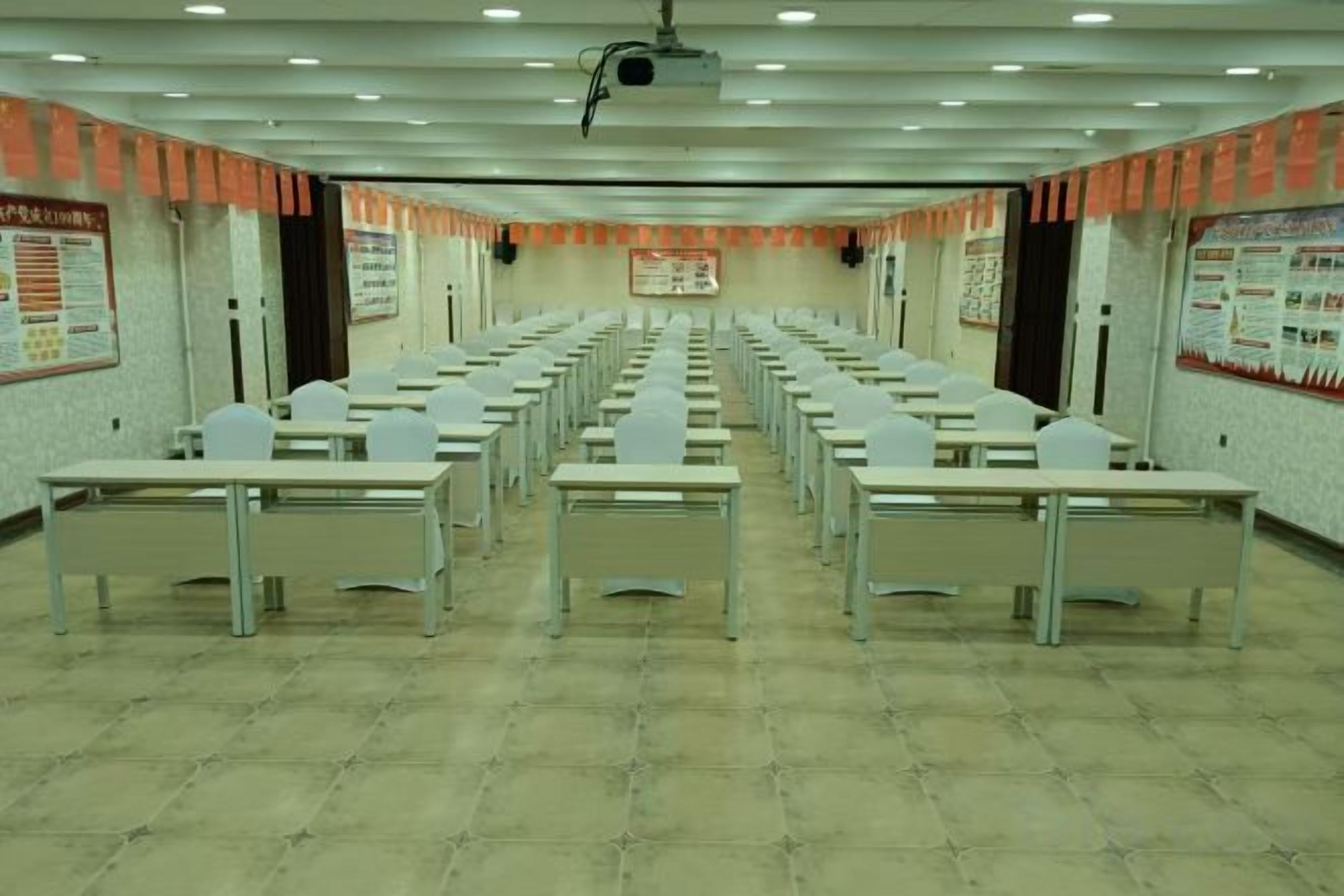 Uma sala de conferências com mesas e cadeiras dispostas em fileiras, um projetor e cartazes informativos nas paredes.