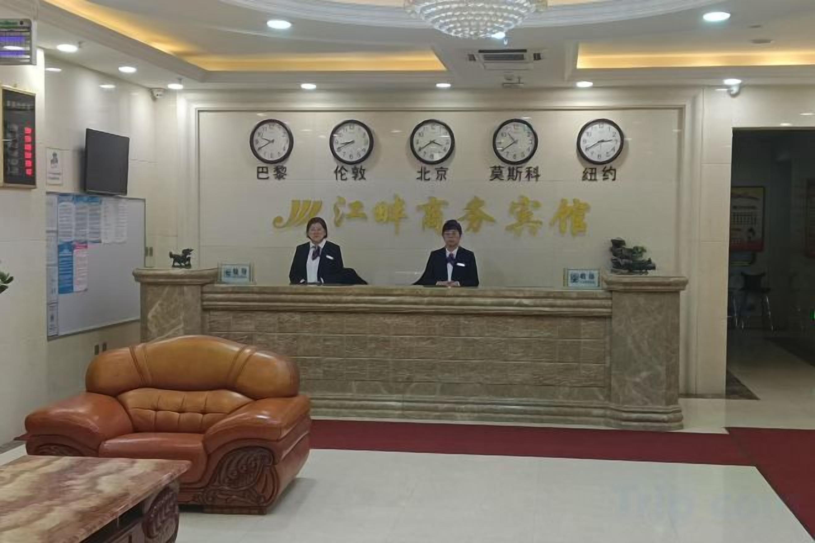Uma área de recepção com balcão, dois recepcionistas, um relógio e uma parede com caracteres chineses.