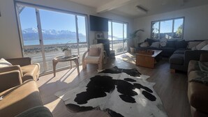 Ampla sala de estar com grandes janelas que oferecem vista para uma paisagem montanhosa e um corpo d'água.