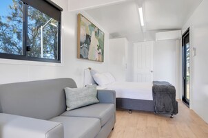 Quarto moderno com sofá cinzento, cama com cobertura cinza, um quadro na parede e janela com vista para árvores.