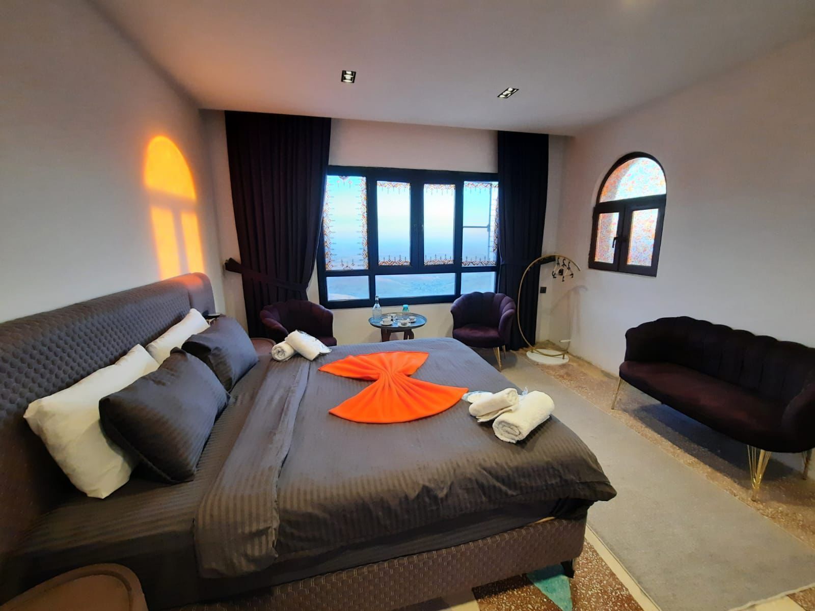 Quarto de hotel com uma cama grande, duas poltronas, uma mesa pequena e um sofá.