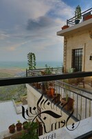 Uma varanda com vasos de plantas, vista para o mar e um edifício com fachada de pedra.