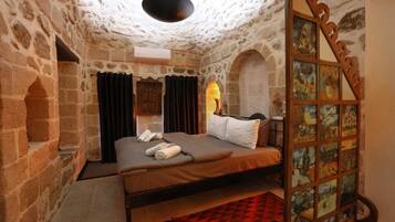 Quarto com paredes de pedra, uma cama, tapete xadrez vermelho e preto e um painel de madeira com obra de arte.