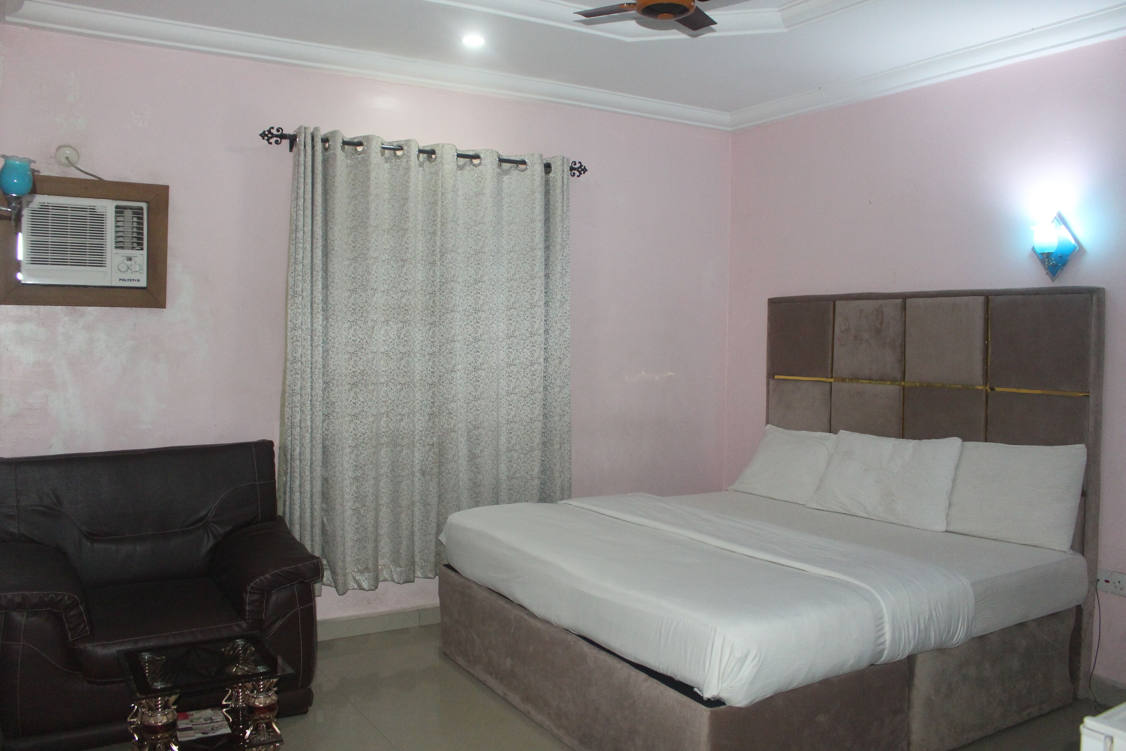 Quarto com cama, sofá, ventoinha no teto e ar-condicionado fixado na parede.