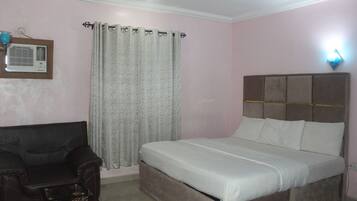 Quarto com cama, sofá, ventoinha no teto e ar-condicionado fixado na parede.