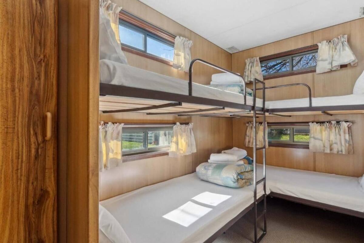 Quarto com beliche, paredes de madeira, janela e cortinas.