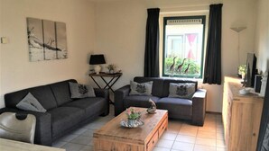 Uma sala de estar com dois sofás, uma mesa de centro, um abajur e uma janela com cortinas.