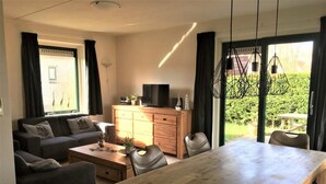 Uma sala de estar com sofá, mesa de jantar de madeira, cadeiras, televisão e um armário.