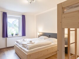 Quarto com cama de madeira, janela com cortinas roxas, abajur e vista para montanhas.