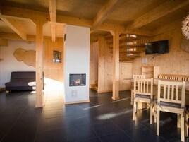 Interior de madeira com lareira, um sofá e uma área de jantar com cadeiras.