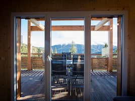 Um deck de madeira com porta de vidro que dá para uma varanda com vista para uma paisagem montanhosa.