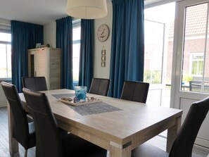 Uma área de refeições com uma mesa de madeira, seis cadeiras, um relógio e cortinas azuis.