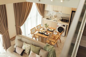 Uma sala moderna com sofá, mesa de jantar e cadeiras, cozinha equipada e janelas amplas com cortinas.