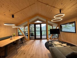 Um quarto amplo com teto de madeira, uma janela grande, uma escrivaninha de madeira, um sofá e uma TV sobre um tripé.